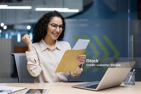 사무실에서 노트북이 있는 책상에서 종이에 좋은 뉴스를 읽으며 성공을 축하하는 여성 쾌활한 표현 전문적인 환경 직장에서의 기쁨 경력 성취 긍정적인 업무 순간 개발에 대한 스톡