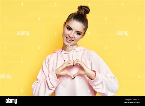 Young Smiling Pretty Woman Making Heart Symbol By Hands On Yellow Background Body Language