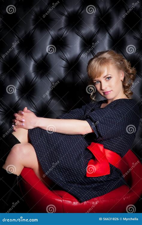 Mädchen Im Schwarzen Kleid Das Auf Einem Roten Stuhl Sitzt Stockfoto