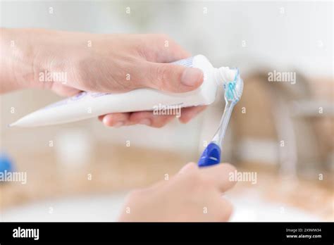 Some Hands Are Squirting Toothpaste Onto A Toothbrush Over The Bathroom