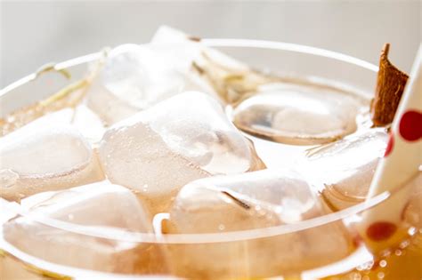 얼음 조각이 있는 유리 컵에 레몬 아이스 티와 대리석 배경에 빨간 공이 있는 흰색 종이 빨대 건강 관리 과일과 식물을 사용한