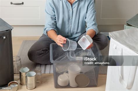 아시아계 혼혈인 젊은 여성이 부엌 바닥에 앉아 재활용품을 별도의 봉투에 꼼꼼하게 분류하고 있습니다 그녀는 플라스틱 재료를 분리하여 적절한 재활용 수거를 준비합니다 0에 대한