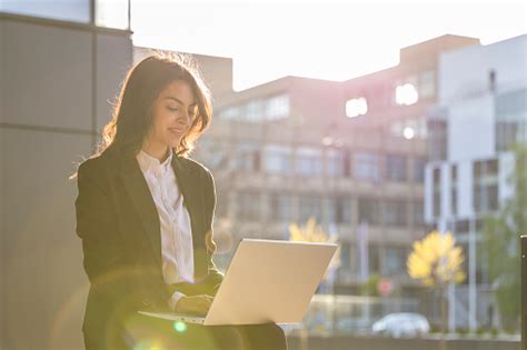 노트북에서 일하는 웃는 여성 사업가 보험 대리인은 컴퓨터에서 이메일을 확인하고 현대 사무실 센터 근처의 야외에 앉아 있습니다