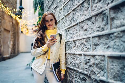 온라인 사교 활동을위한 이동성 시간 동안 벽에 서서 웃고있는 교육 장비를 손에 들고 행복한 여성 블로거의 초상화 스마트 폰