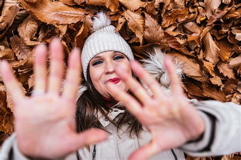 모직 모자를 쓴 젊은 여성이 밤나무 숲의 나뭇잎 담요 위에 누워 웃고 카메라를 바라보며 손을 잡고 있다 가을에 대한 스톡 사진 및 기타 이미지 Istock