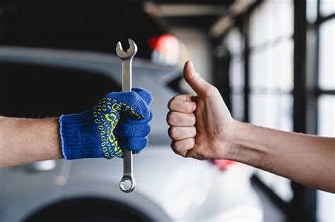 밀폐 된 크롭 샷은 기술자 정비사 손에 렌치를 자르고 남성의 손이 엄지 손가락을 들고 있습니다 Mot 차량 검사 차고 워크샵 주유소에서 자동차 타이어 바퀴 고정 수리 석유에