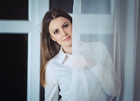 Woman Peek Out From Behind White Curtain Near The Window Stock Image