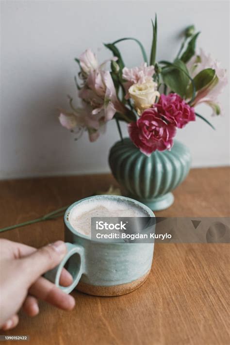 소박한 나무 배경에 커피와 꽃의 세련된 세라믹 컵을 들고 손 분홍색 꽃과 현대적인 커피 컵이있는 세라믹 꽃병 봄 아침 미학