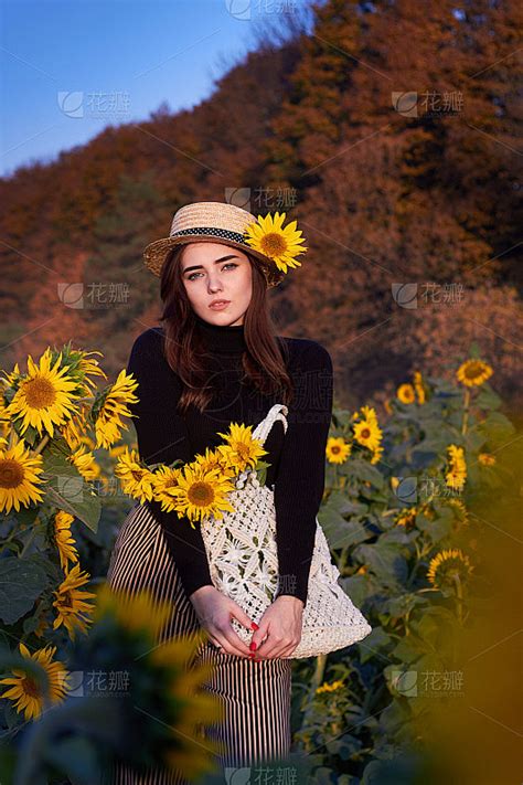 漂亮可爱的女孩戴着草帽，拿着一个柳条包，里面插着花。在阳光明媚的向日葵地里享受大自然。秋天的时间。幸
