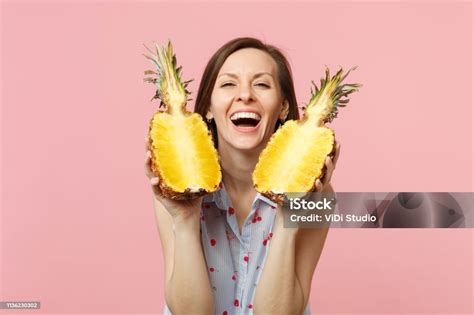 스튜디오에서 분홍색 파스텔 벽 배경에 고립 된 신선한 잘 익은 파인애플 과일의 Halfs를 들고 여름 옷에 젊은 여자를 웃 고 사람들은 생생한 라이프 스타일 휴식 휴가