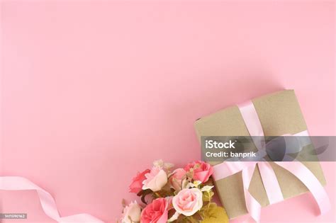 파스텔 핑크 배경에 핑크 새틴 곱슬 리본 활이있는 갈색 종이 선물 상자 플랫 레이 어머니의 날 아버지의 날 발렌타인 데이 복사 공간이있는 생일 개념 0명에 대한 스톡 사진