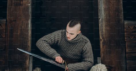 검을 갈고 있는 강한 바이킹 전사의 초상화 스칸디나비아 바이킹 코스프레 겨울 숲의 늑대 가죽에 앉아 강철 검을 든 중세 전사 전투 준비 개념 사진 Unsplash의