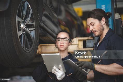 안전 안경과 손장갑이 달린 유니폼을 착용하고 자동차의 문제를 진단하면서 디지털 태블릿에서 작업하는 젊은 남성과 여성 자동차 정비사 자동차 수리 공장에 대한 스톡 사진 및