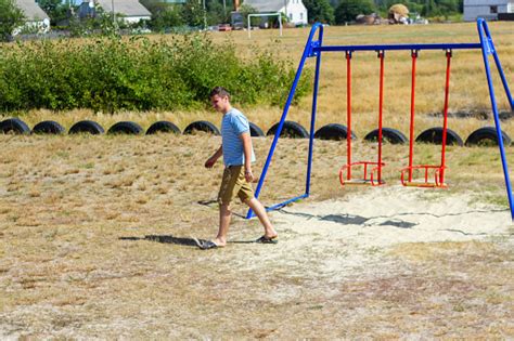 시골 지역 배경에 놀이터에 디포커스 스윙 놀이터를 따라 지나가는 청년 밝은 파란색과 빨간색 스윙 가족 여름 게임 포커스가
