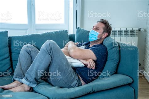 코로나바이러스 사망 직장 분실 잠금 및 사회적 불변으로 인해 피곤하고 걱정스러운 고통을 느끼는 집 거실 소파에서 보호 얼굴 마스크를 쓴 슬픈 남자 정신 건강과 격리 개념