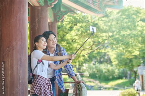 한국의 옛날 전통 가옥의 처마와 녹색 숲을 배경으로 여행하며 스마트폰으로 다양한 포즈를 셀카로 찍는 젊은 아시아 한국 남녀 모델 Stock 사진 Adobe Stock