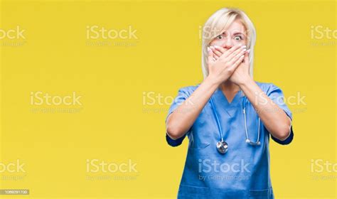 젊은 아름 다운 금발 의사 여자 입 실수에 대 한 손으로 다루는 충격된 절연된 배경 위에 의료 유니폼을 입고 비밀 개념입니다
