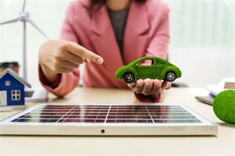 분홍색 양복을 입은 사업가가 세계 모형 전기 자동차 모형 녹색 전구가 있는 흰색 책상 앞에 서서 지구의 날 녹색 에너지 및 지속 가능성 노력을 홍보합니다 감소에 대한 스톡