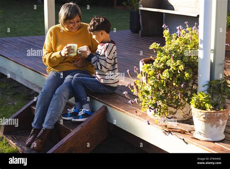 Happy Biracial Grandmother And Grandson Drinking Tea Sitting In Garden Copy Space Stock Photo