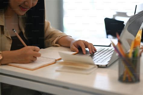 웃고 있는 큐비 소녀가 컴퓨터 노트북으로 작업하고 노트북에 메모를 하는 장면이 잘립니다 사진 Unsplash의 앉아 이미지