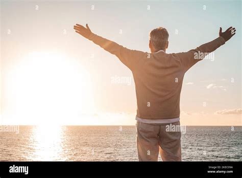 Old Man Looking To The Sunset And The Sea With Opened Arms Feeling Free