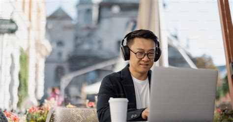 카페에서 일하는 동안 이어폰을 끼고 노트북에 타이핑을 하는 아시아 사업가 원격 및 프리랜서 작업의 개념입니다 양복을 입고 커피와 함께 테이블에 앉아 있는 성공한 성인