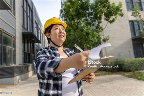 젊은 건물 검사관이 옥외 건축 구조물을 점검하고 있다 안전모를 쓴 여성 건설 노동자가 도시 배경에 클립보드 체크리스트를 들고 서 있다 전문 아키텍처 감사 개발에 대한 스톡