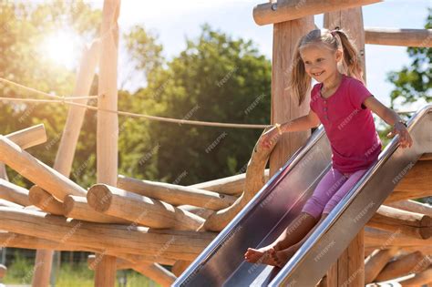 놀이터에서 미끄럼틀을 타는 어린 소녀 아이가 현대 나무 놀이터에서 미끄럼틀 그네를 타고 있습니다 프리미엄 사진