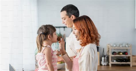 아시아의 매력적인 부모는 부엌에서 귀여운 딸에게 컵케이크를 먹인다 행복한 가족 사랑하는 부부 베이킹 집에서 점심을 먹기 위해 카운터에 앉아있는 동안 작은 귀여운