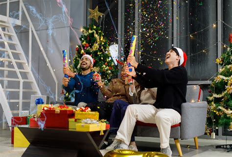 그룹 아시아 인도 행복 쾌활 한 남성 여성 친구 착용 빨간 산타 클로스 모자 순록 뿔 머리띠 촬영 반짝이 색종이 소파 함께 장식 거실에서 크리스마스 이브를 축하 아시아에