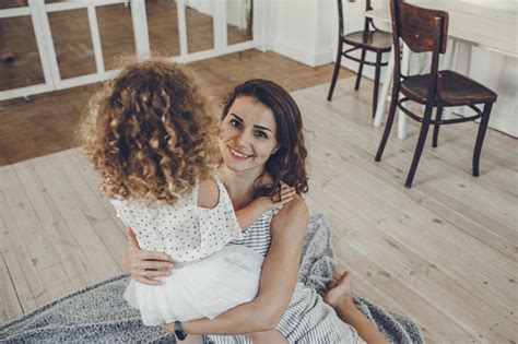 엄마는 딸과 함께 집에서 시간을 보낸다 귀여운 어린 딸이 거실 바닥에 앉아있는 쾌활한 젊은 어머니를 껴안습니다 어머니와 자식 개념 유머에 대한 스톡 사진 및 기타 이미지