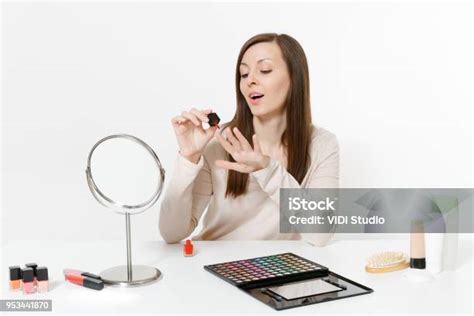 아름 다운 젊은 여 자가 그림을 흰색 배경에 고립 설정된 얼굴 장식 화장품으로 메이크업을 적용 하는 테이블에 앉아 빨간 매니큐어와 손톱 뷰티 여성 패션 라이프 스타일