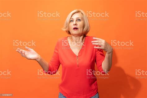 금발 머리를 가진 아름다운 중년 여성의 절반 길이 초상화는 주황색 배경에 고립 된 포즈를 취합니다 감정의 개념 얼굴 표정 55 59세에 대한 스톡 사진 및 기타 이미지