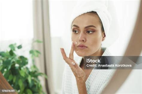 바스티고를 손에 들고 머리에 수건을 든 아름다운 젊은 여성이 얼굴에 문제가 있는 피부를 위해 크림을 바른다 피부 관리의 개념 보습 및 얼굴과 목을 클렌징 여드름에 대한 스톡