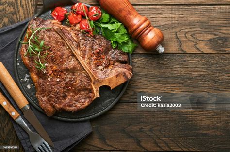 스테이크 티본 얇게 썬 쇠고기 구운 Tbone 또는 포터 하우스 고기 스테이크와 향신료 로즈마리와 후추는 오래 된 나무 배경에 검은 대리석 보드에 있습니다 평면도 모의 0