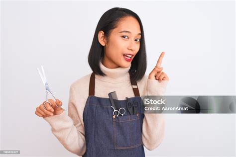 중국 미용사 여자 에이프런 을 입고 가위를 들고 고립 된 흰색 배경 에 놀란 아이디어 또는 질문 가리키는 손가락으로 행복한 얼굴 번호 하나 가리키기에 대한 스톡 사진 및
