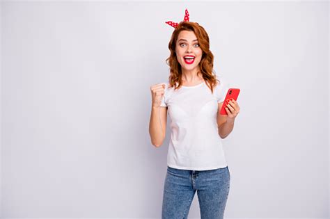흥분 미친 여자 사용 스마트폰 승리 온라인 소셜 네트워크 복권 비명 Yeas 제기 주먹을 착용 데님 티셔츠 를 통해 고립 된 흰색 배경 T 셔츠에 대한 스톡 사진 및 기타