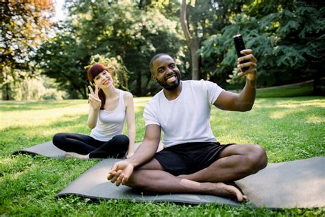 공원에서 요가 재미있는 젊은 다민족 가족 커플이 Youga를 준비하고 야외에서 운동하고 맞는 매트에 앉아 스마트폰으로 사진을 찍는 수평 사진 건강한 라이프 스타일의