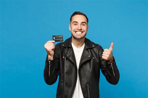 검은 가죽 자 켓 흰색 T 셔츠에 잘생긴 세련 된 젊은 면은 남자 파란색 벽 배경 스튜디오 초상화에 고립 된 손에 신용 카드를 개최 합니다 사람들 라이프 스타일 개념입니다