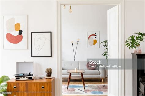 디자인 회색 소파 레트로 테이블 램프 및 가구와 세련 된 복고풍 거실 흰 벽에 포스터 프레임을 비웃는 다 갈색 나무 마루와 최소한의 방입니다 가정 생활에 대한 스톡 사진 및