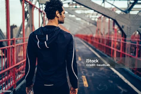 브릿지 서딩 운동에 서있는 스포츠웨어 라벨의 브랜드 이름이 있는 트랙수트를 입은 현대 이어폰의 핏 맨의 뒷모습 윈드 브레이커 재킷을 입은 남성의 뒷모습과 모의 영역 듣기에