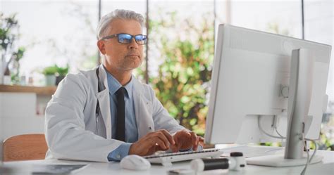 일상적인 병원 운영을 위해 데스크톱 컴퓨터를 사용하는 의료 의사 공공 의료 시설의 현대적인 사무실에서 효율적인 온라인 의료 작업을 위해 Pc를 사용하는 클리닉 전문가