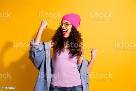 기쁘게 긍정적 인 소녀 의 초상화 제기 주먹 예 경쟁 착용 데님 청바지 재킷 핑크 탱크 탑 노란색 색상 배경 위에 승리를 축하