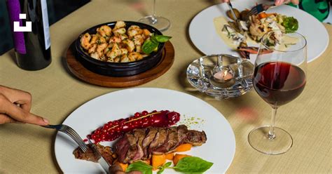 녹색과 흰색 꽃무늬 셔츠를 입은 사람이 음식과 함께 테이블 옆에 앉아 있다 사진 Unsplash의 무료 마시다 이미지