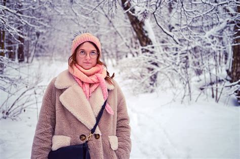하얀 모피 코트와 분홍색 모자를 쓴 한 여성이 눈 덮인 겨울 숲에 서 있다 공원 나무 사이에 안경과 가방을 가진 성인 여성의 초상화 30 34세에 대한 스톡 사진 및 기타