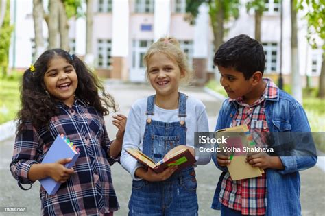 학교로 돌아갑니다 배낭을 들고 학교 앞에서 포옹하고 웃으며 세 친구를 가까이에 두세요 학교 마당에서 재미를 갖는 학교 아이들의 혼합 인종 그룹 고등학교 이하에 대한 스톡