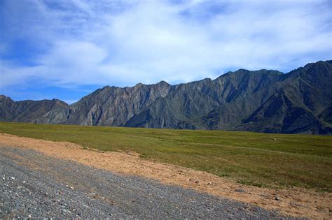 하얀 적운 구름이 있는 푸른 하늘 아래 높은 언덕 기슭에 신선한 잔디가 있는 목초지를 가로지르는 비포장 도로 0명에 대한 스톡 사진 및 기타 이미지 Istock