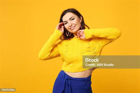 스웨터에 즐거운 젊은 여자의 초상화 파란색 바지 카메라를 찾고 노란 오렌지 배경에 고립 된 얼굴 가까이 손을 유지 사람들은