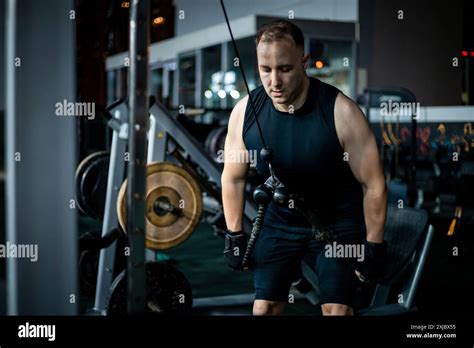 A Man In A Gym Works Out Using A Cable Machine Pulling Down On A Cable With A Weight Attached