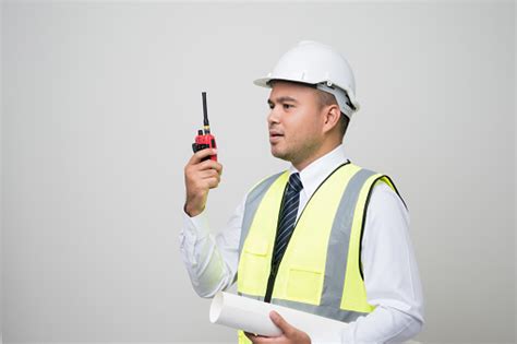 아시아 토목 엔지니어는 스튜디오에서 작업을 제어하기 위해 라디오 무전기와 함께 작동합니다 고립된 흰색 배경에 단단한 모자를 쓰고 있는 작업자 개발에 대한 스톡 사진 및 기타